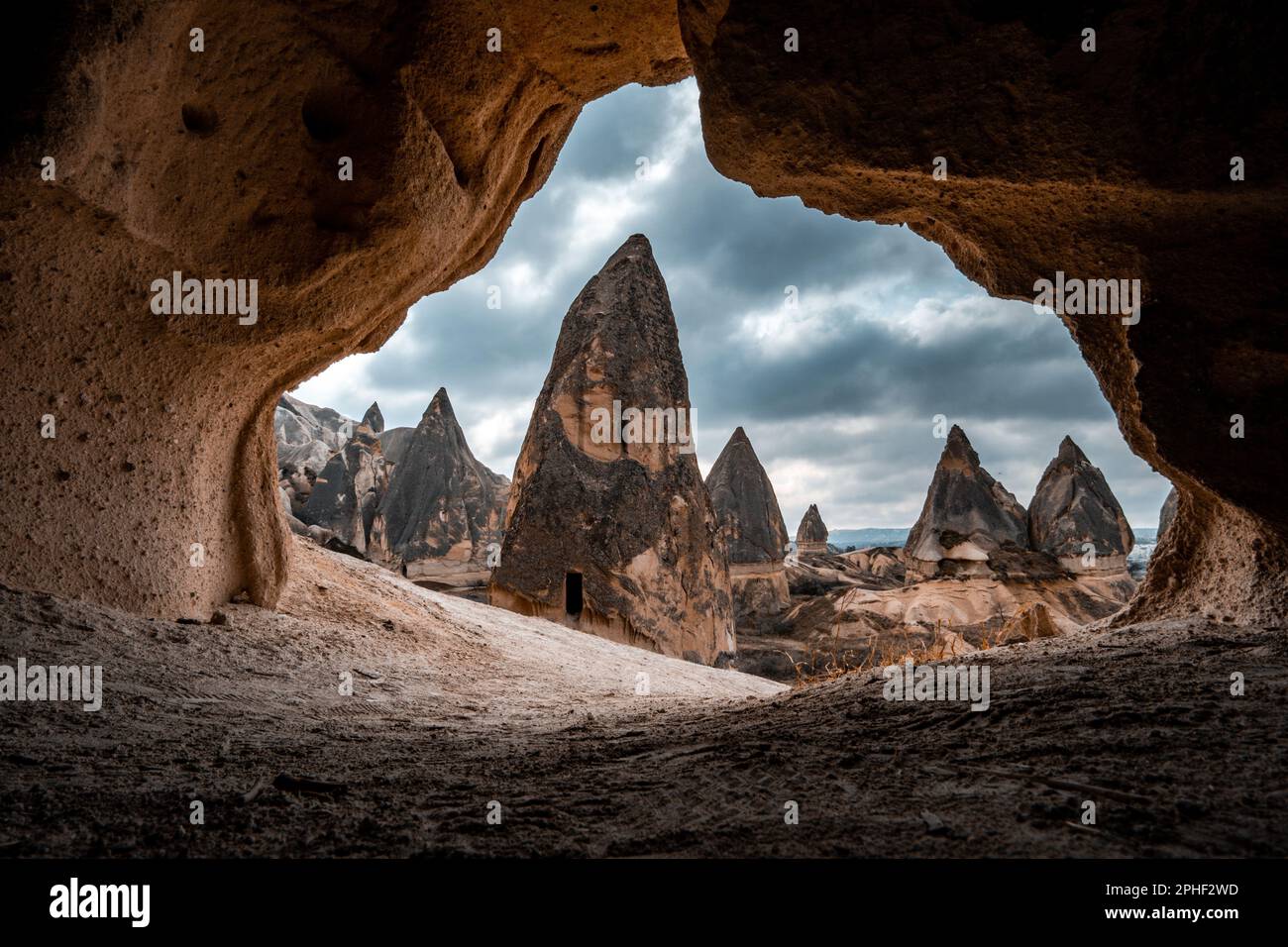 A dramatic landscape featuring a cave filled with rust-colored rock ...