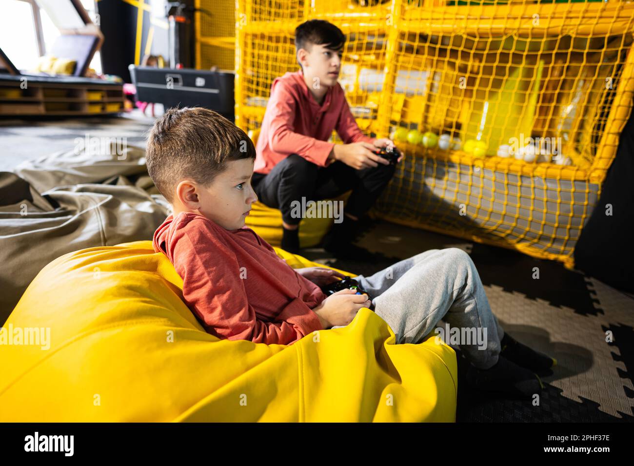 Two brothers playing video game console, sitting on yellow pouf in kids ...