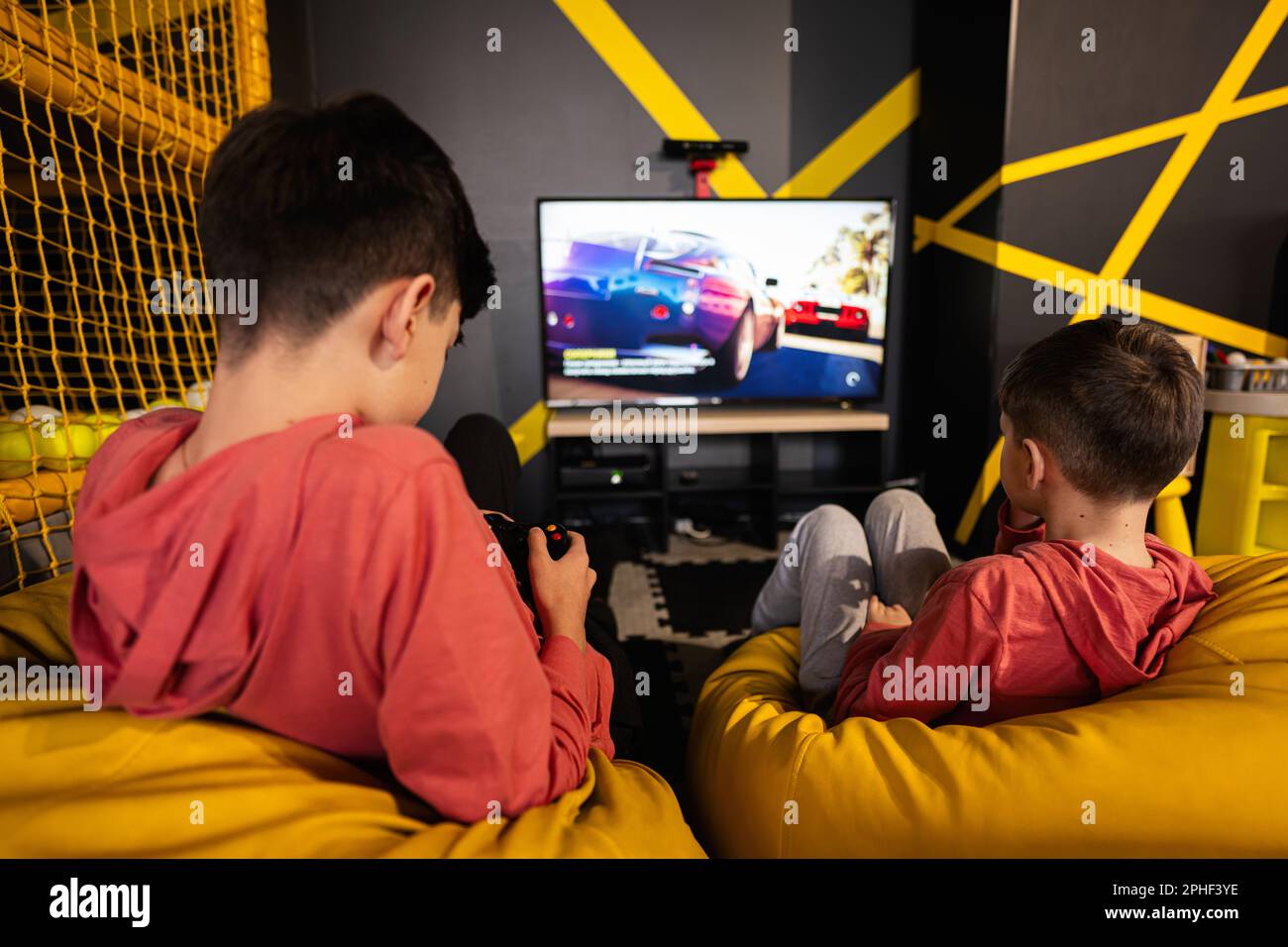 Two brothers playing race video game console, sitting on yellow pouf in ...