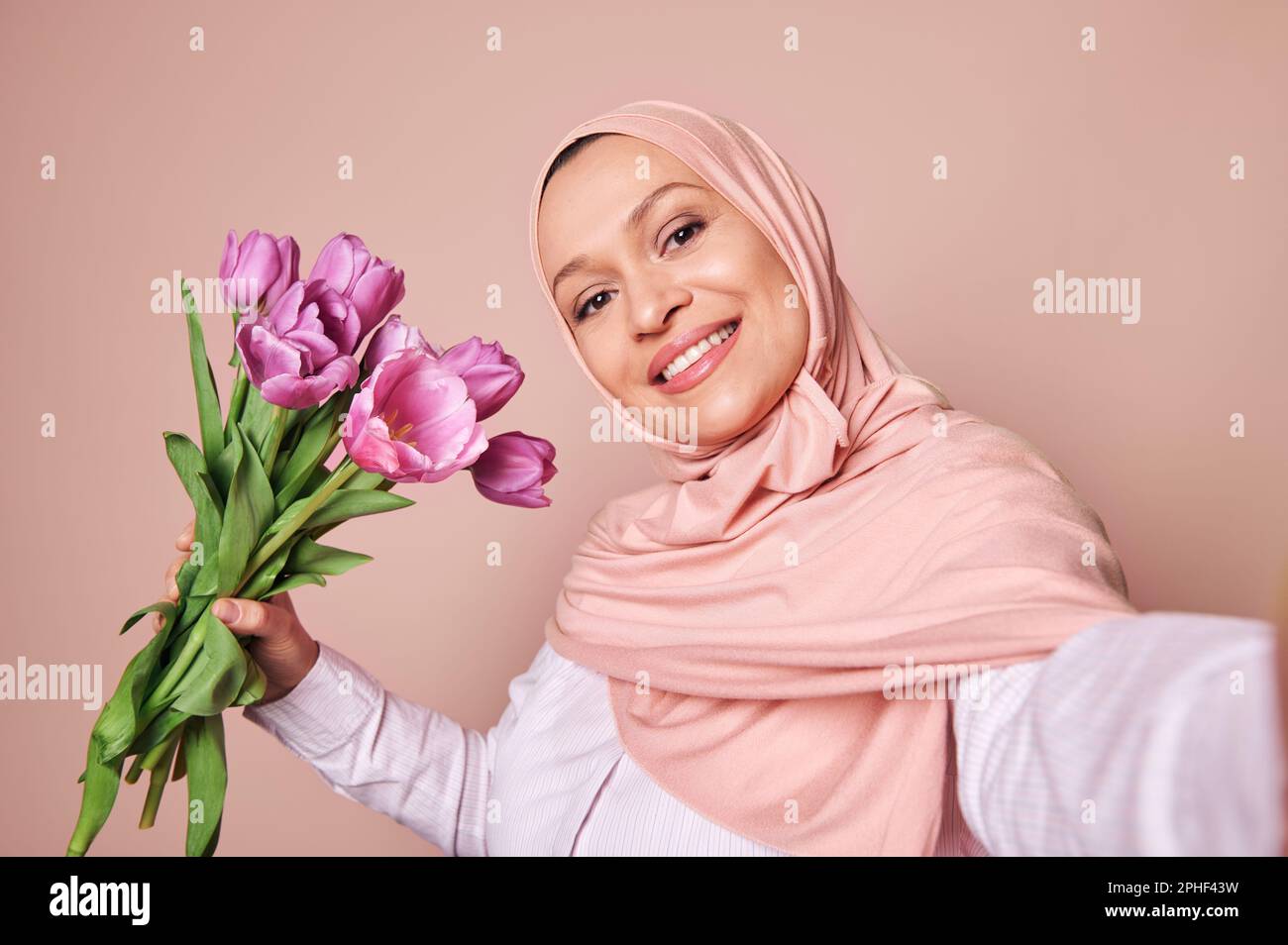 Self-portrait of Muslim woman holding bouquet of tulips, smiling at web ...