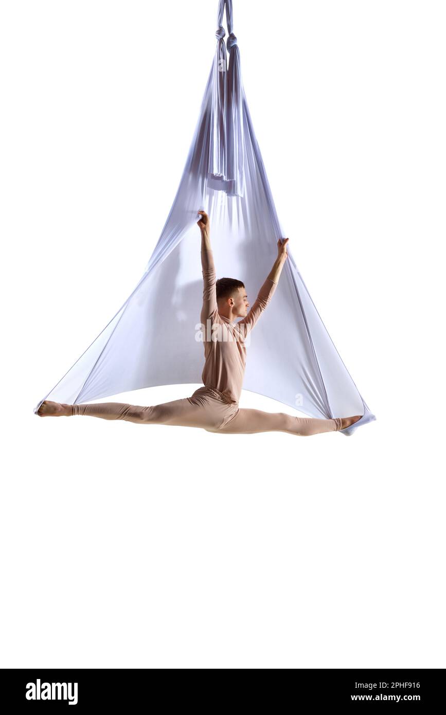 Sportive young man hanging in silk hammock in twine position, training ...