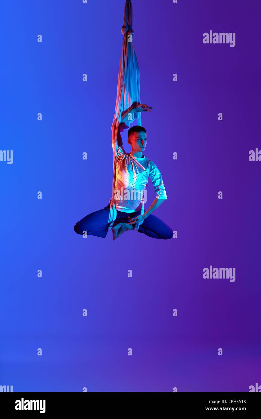 Male acrobat, professional, artistic aerial gymnast hanging upside down ...