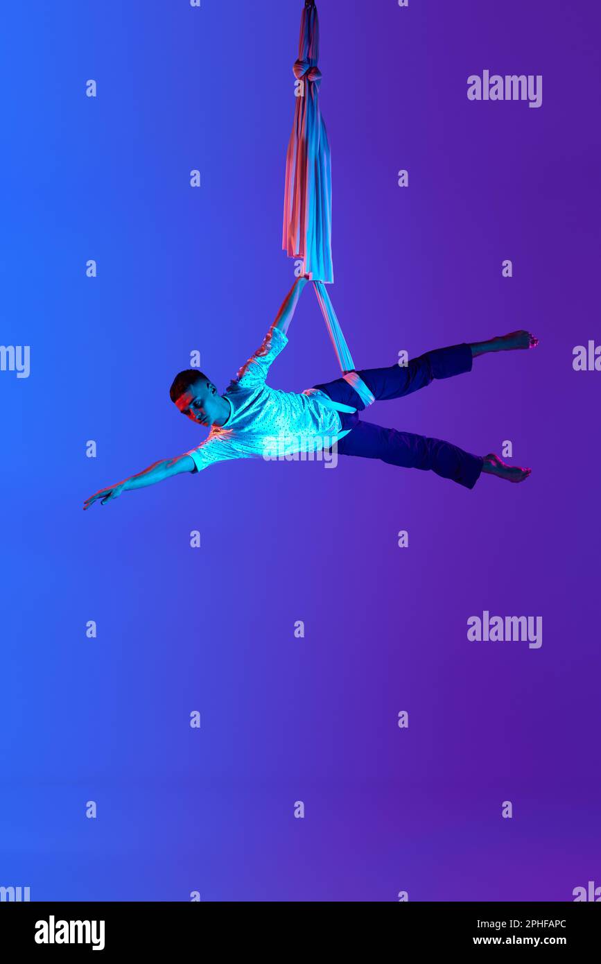 Acrobat, professional male aerial gymnast hanging upside down on aerial ...