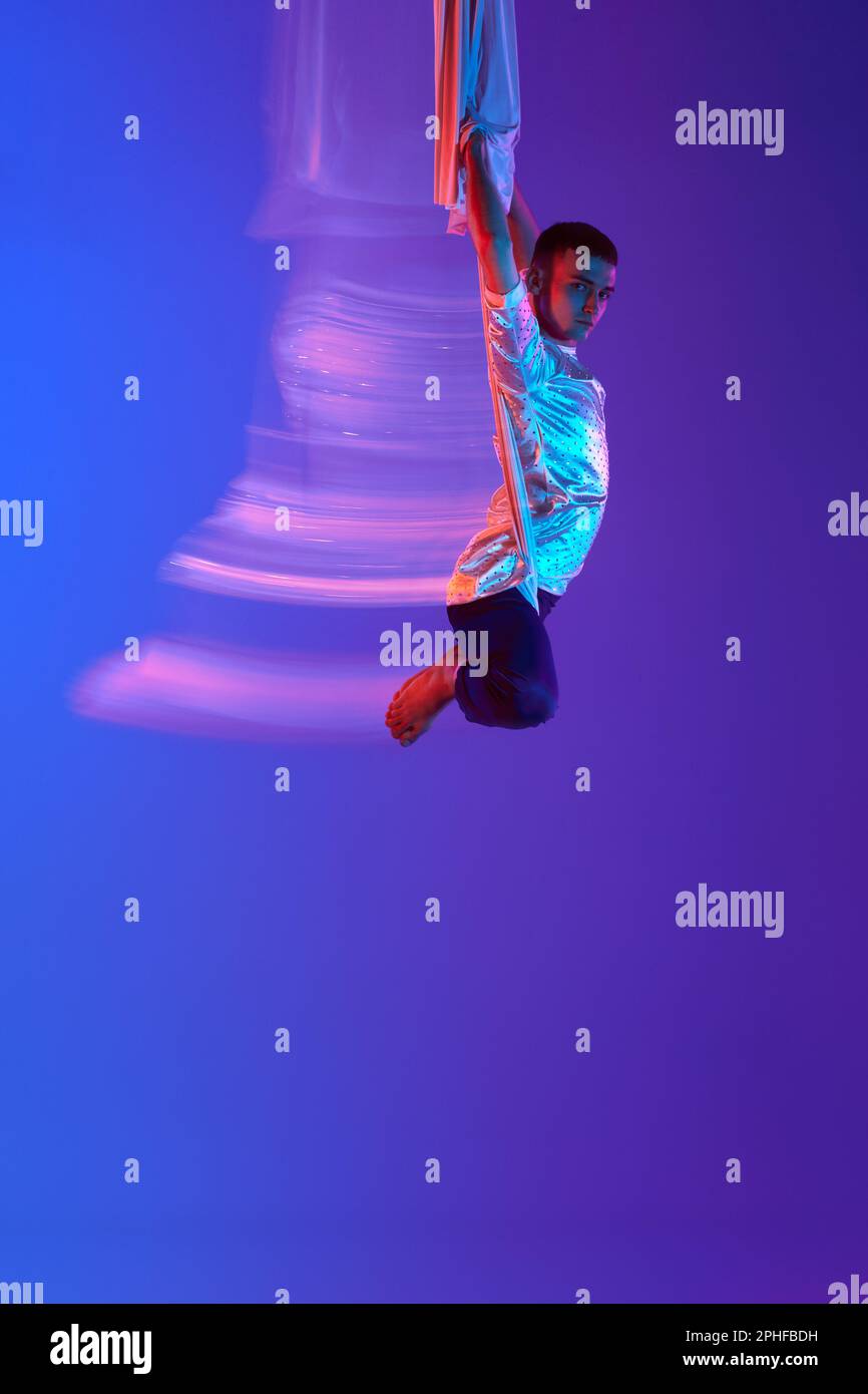 Young man, aerial gymnast, acrobat training with aerial tissue against ...