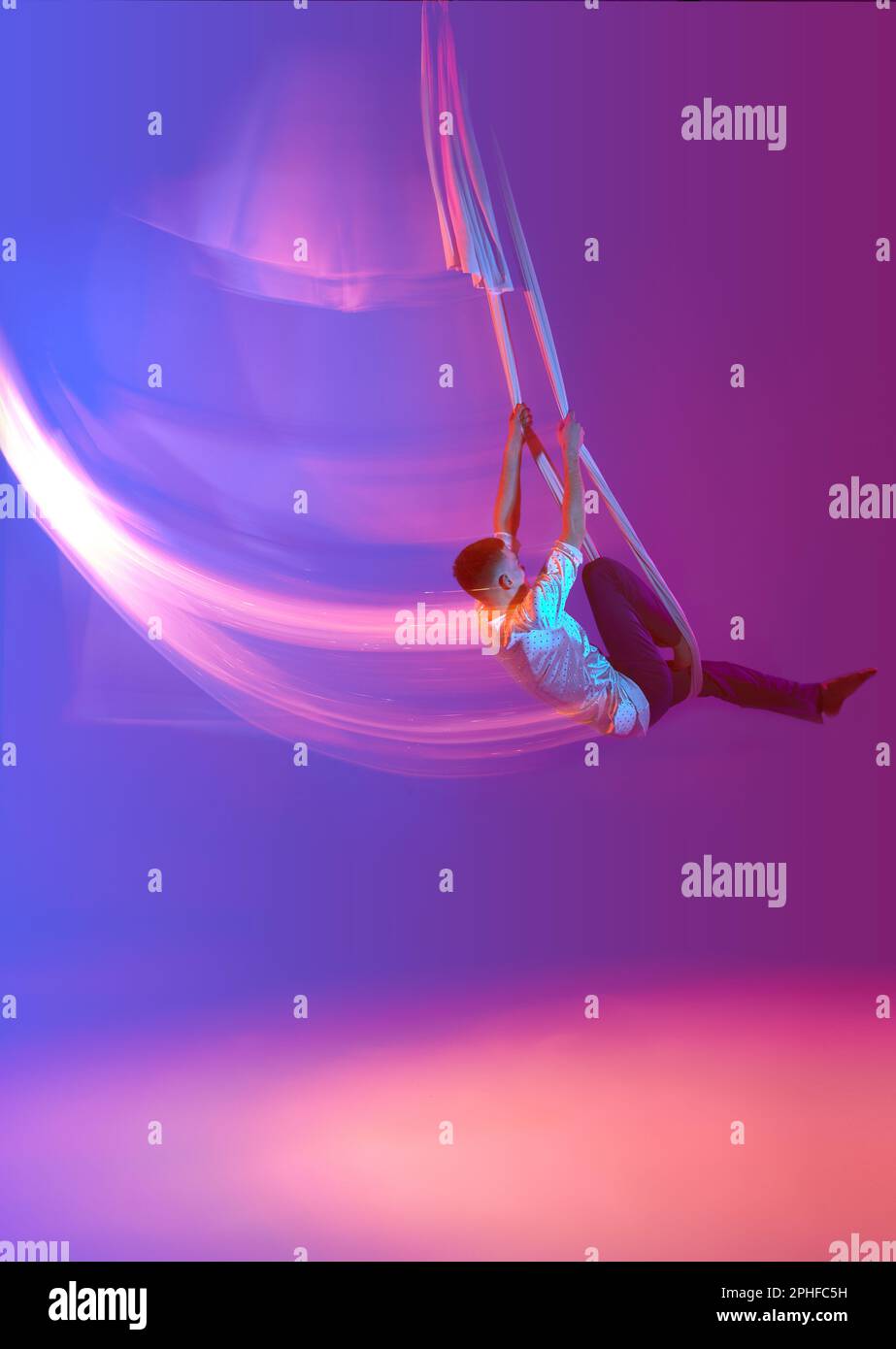 Young man, acrobat training with aerial ribbons against gradient blue ...