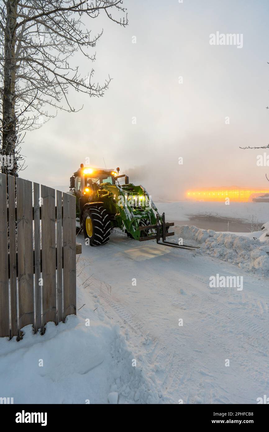 Green tractor removing snow from the road or street with the shovel ...