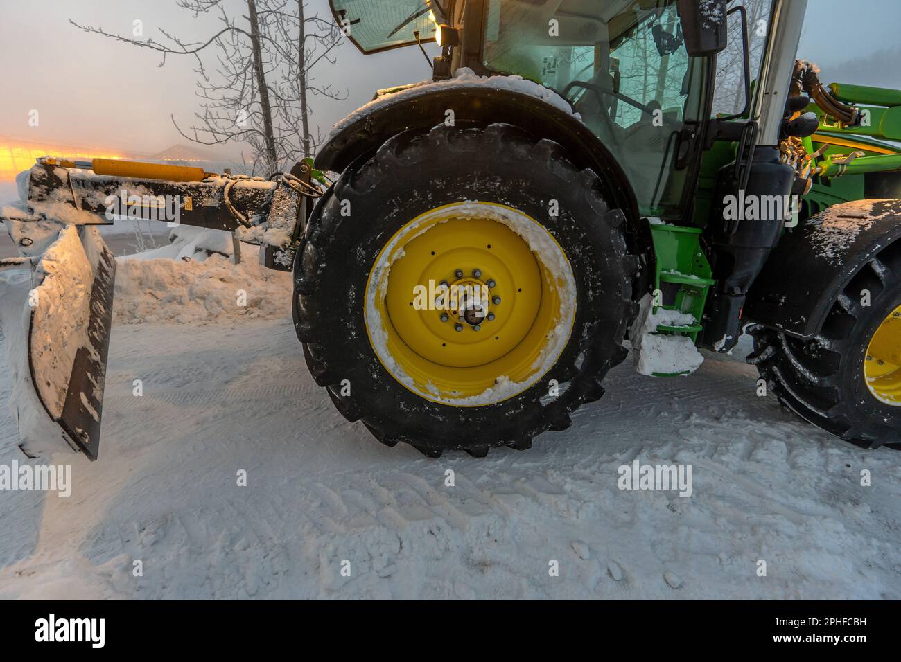 Green tractor removing snow from the road or street with the shovel ...