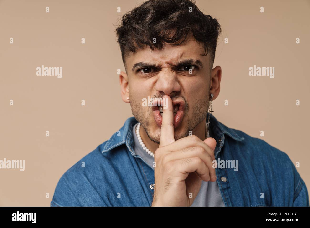 Brunette young man grimacing and showing silence gesture at camera ...