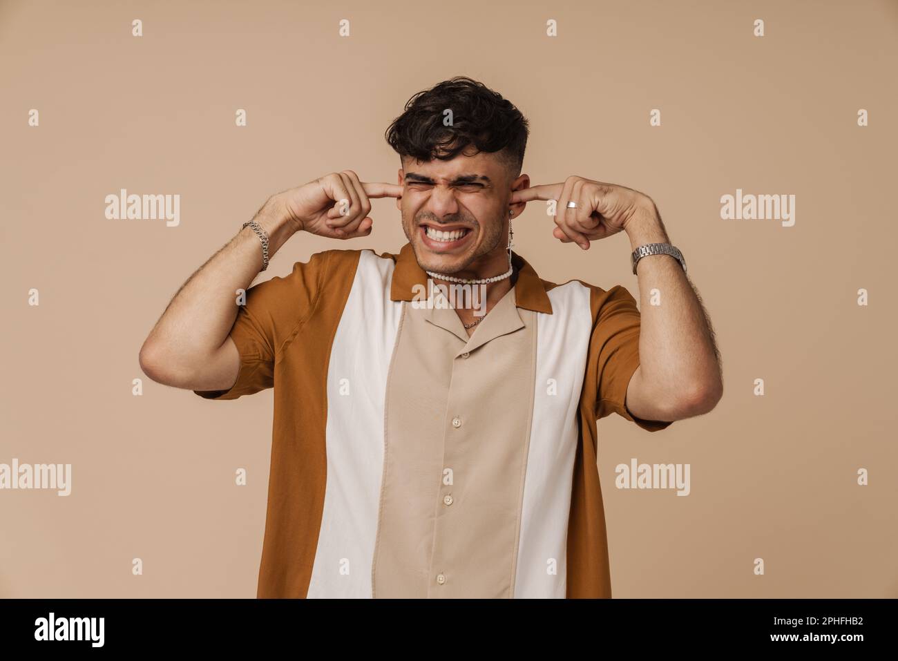 Brunette young man grimacing while plugging his ears isolated over ...