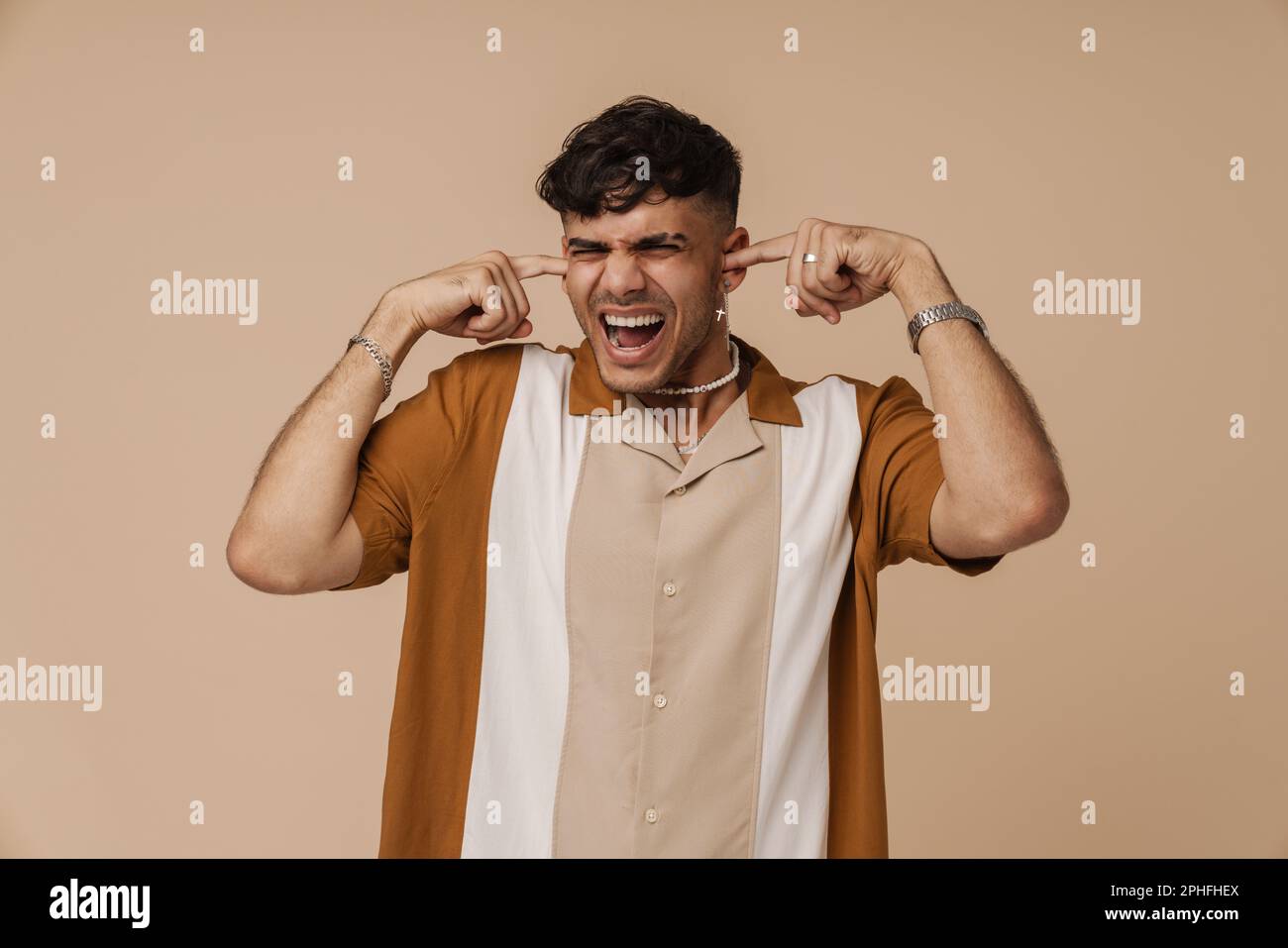 Brunette young man screaming while plugging his ears isolated over ...