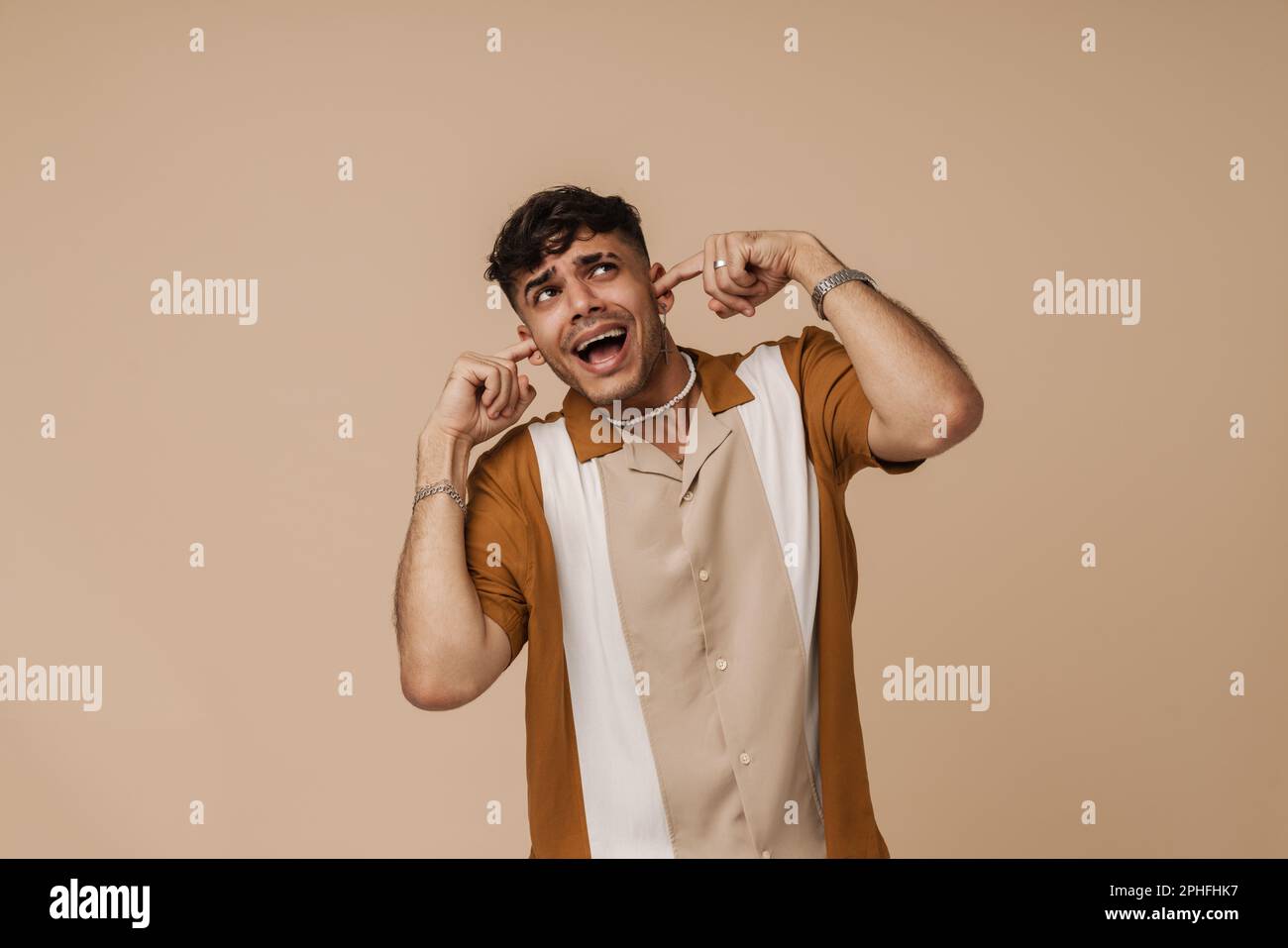 Brunette young man screaming while plugging his ears isolated over ...