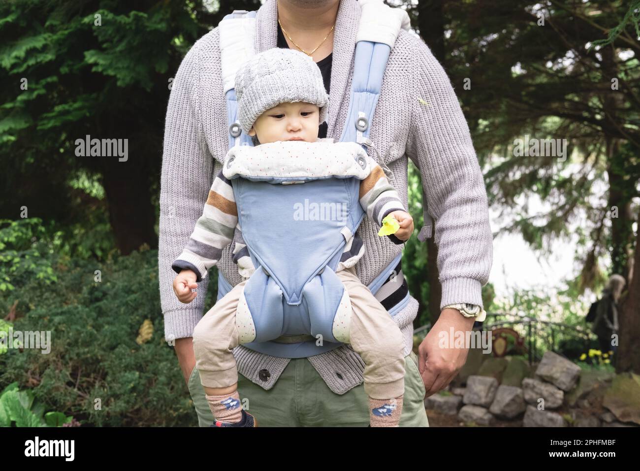 An unrecognizable parent carrying his male infant with a baby carrier ...