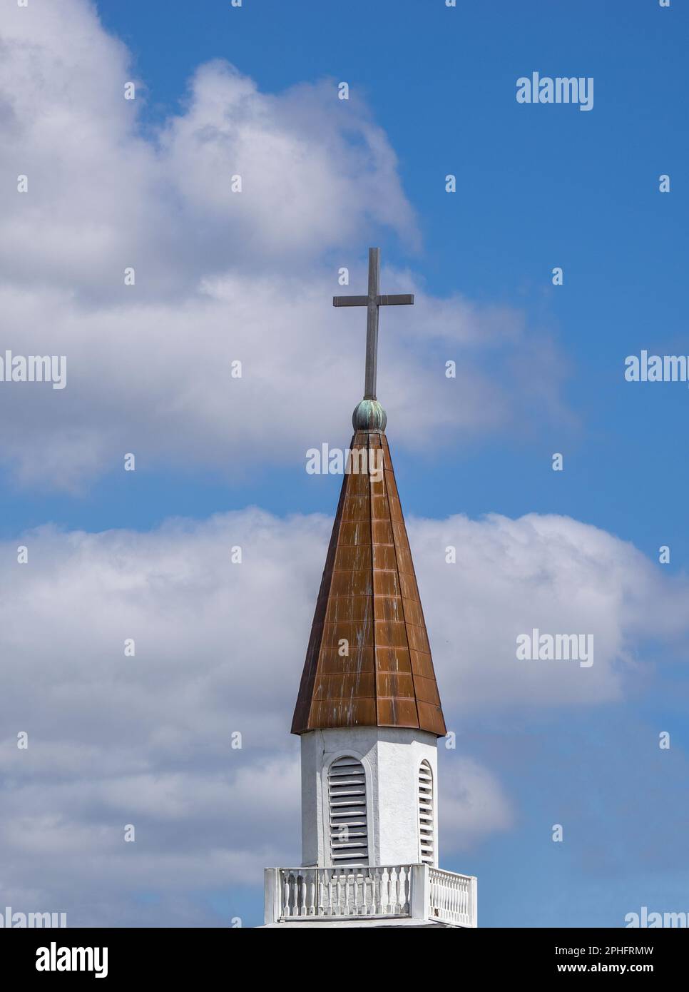 Church steeple with cross on top aganist a blue sky with white clouds ...