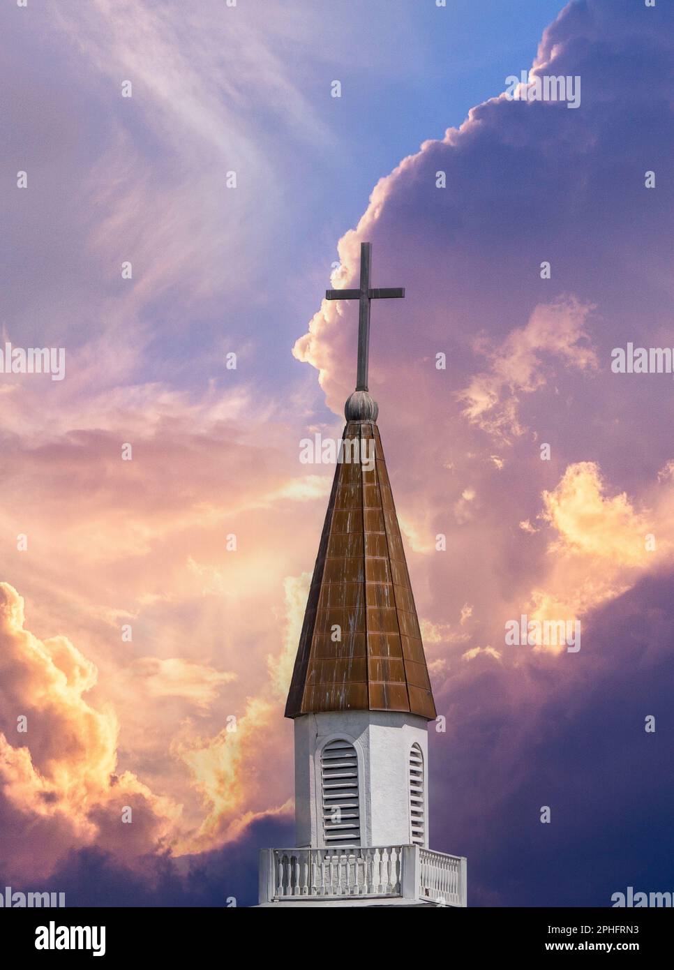 Church steeple with cross on top aganist a light streaked dramatic sky ...