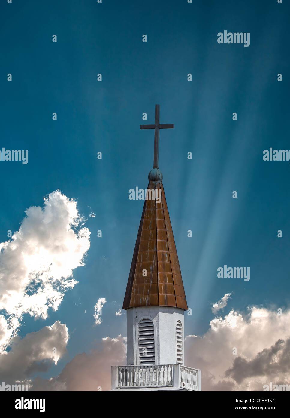 Church steeple with cross on top aganist a light streaked dramatic sky ...