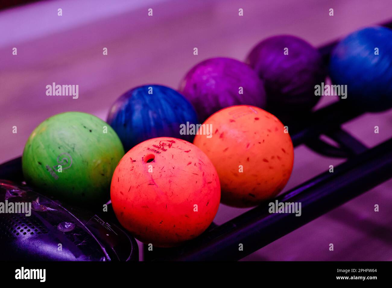 A rack filled with a colorful assortment of rainbow-hued bowling balls ...