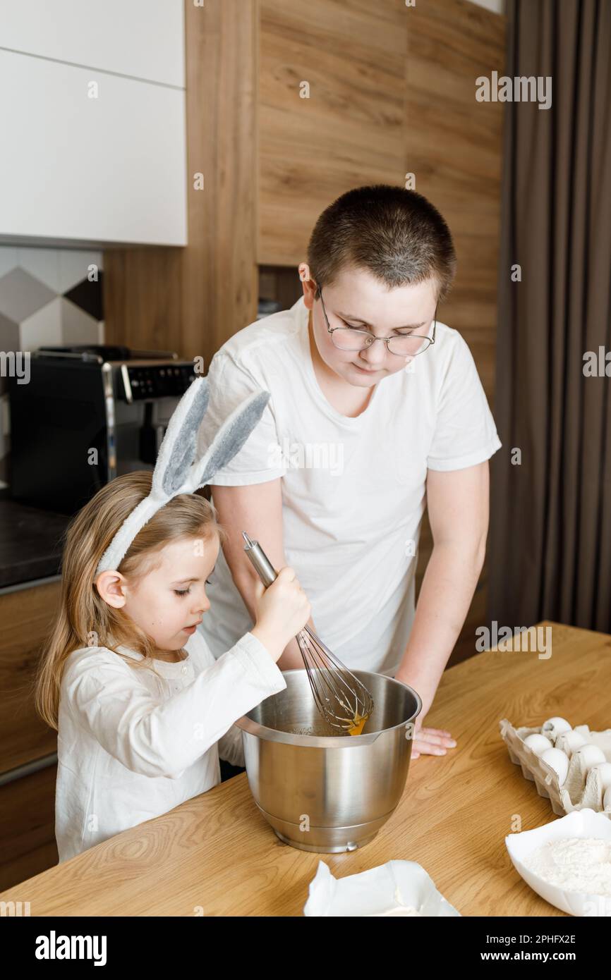 Brother teaching sister cooking, child mixing dough in bunny ears in ...
