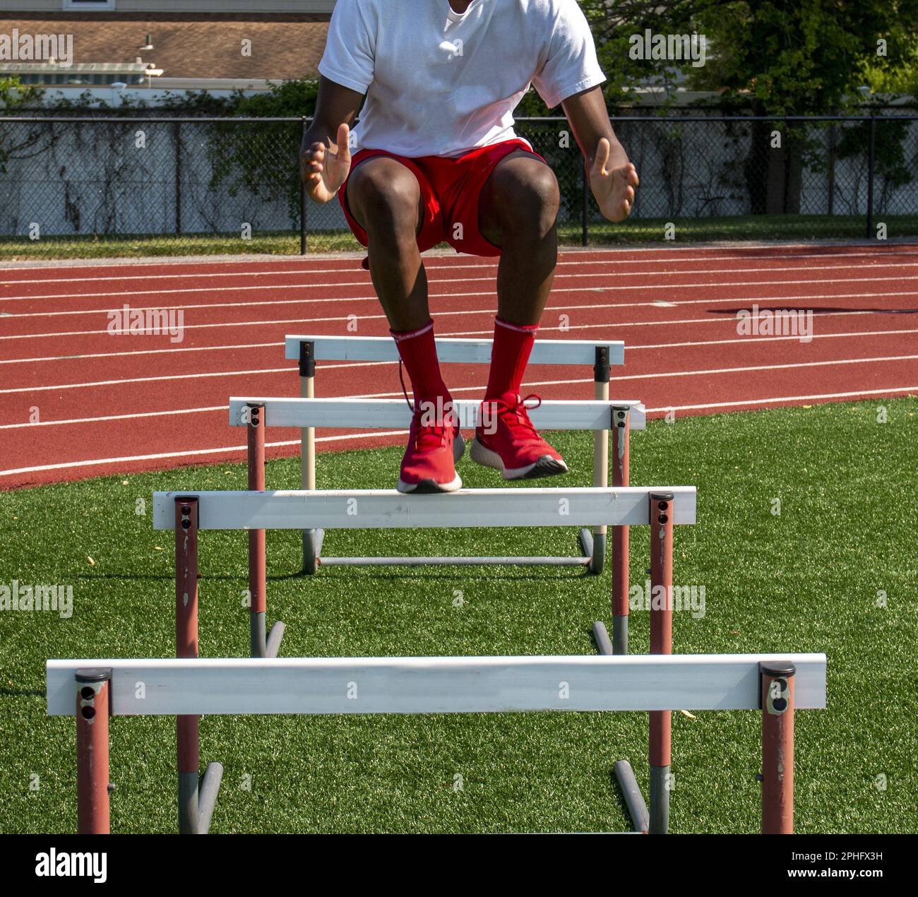 Front view of a high school boy jumping over track hurdles for strength ...