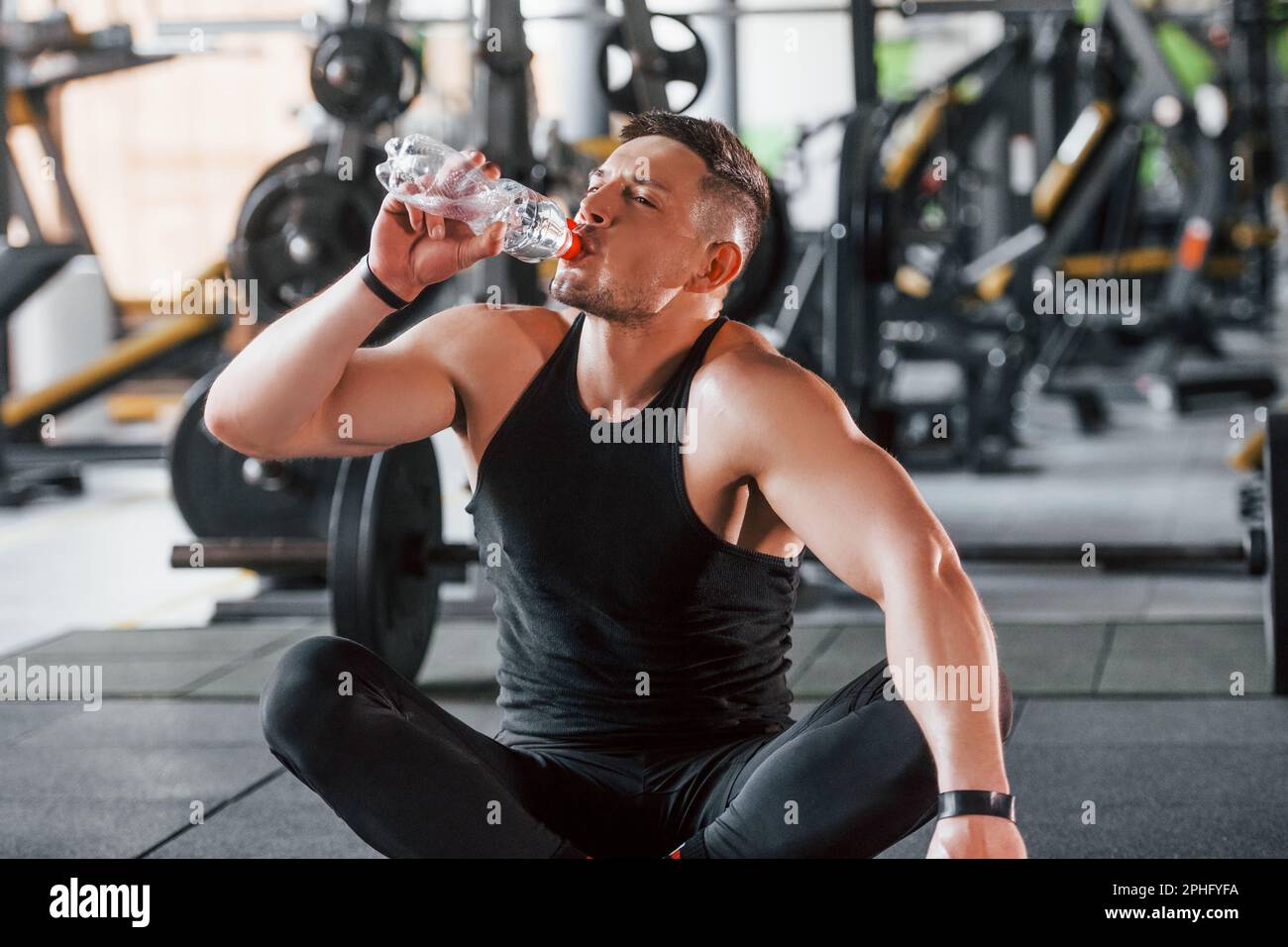 Taking a break and drinking water. Young sportive strong man in black ...