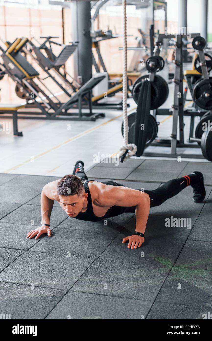 Doing push-ups. Young sportive strong man in black wear have workout ...