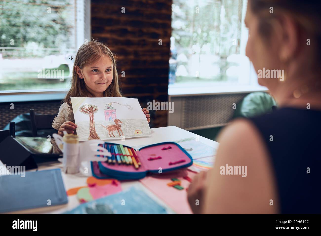 Girl presenting her artwork teacher. Woman assisting schoolgirl during ...