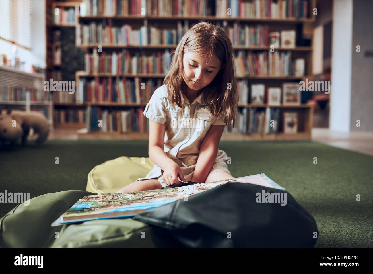 Schoolgirl doing puzzle and reading book in school library. Primary ...