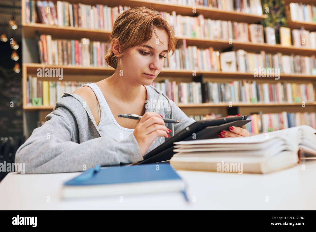 Student learning in university library. Young woman writing essay and ...