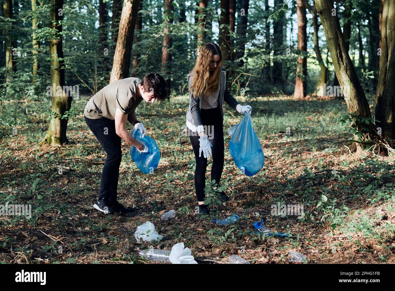 Young man and woman cleaning up a forest. Volunteers picking plastic ...