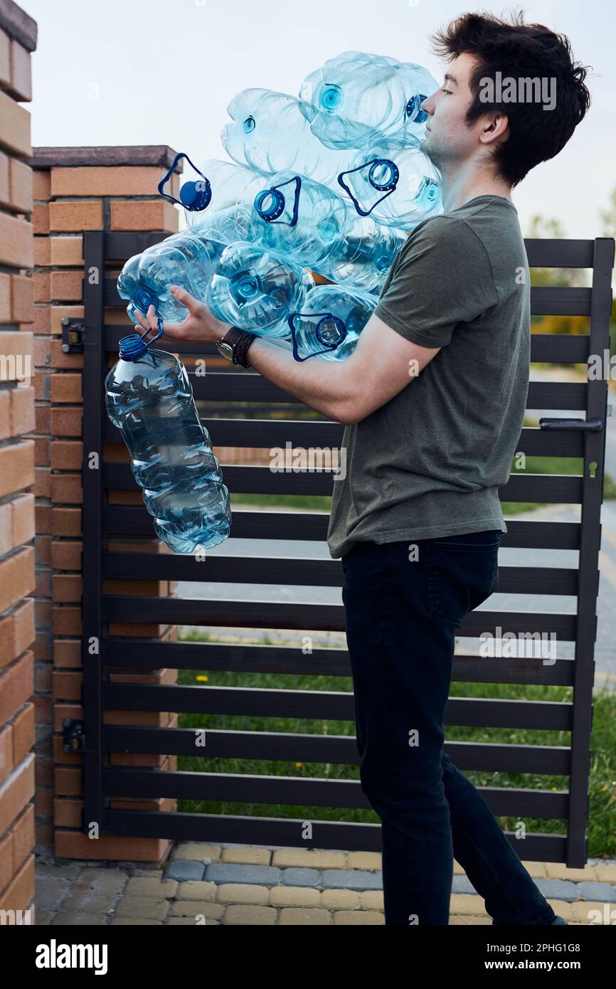 Young man throwing out empty used plastic water bottles into trash bin ...