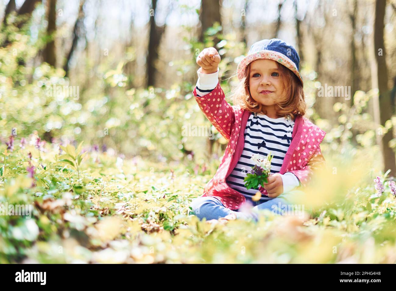 Happy little girl in blue hat have walk in spring forest at daytime ...