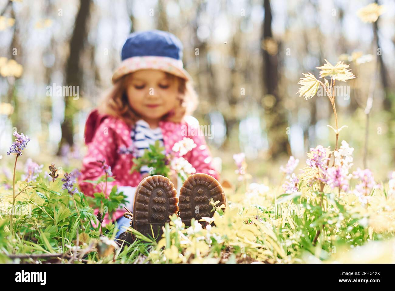 Happy little girl in blue hat have walk in spring forest at daytime ...
