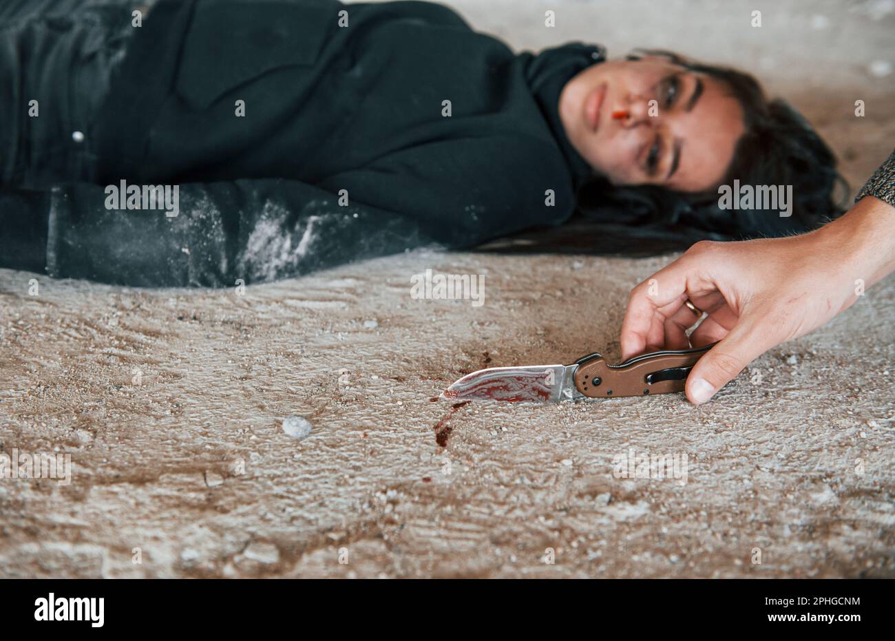 Man's hand holds knife. Corpse of female victim of crime lying down on ...