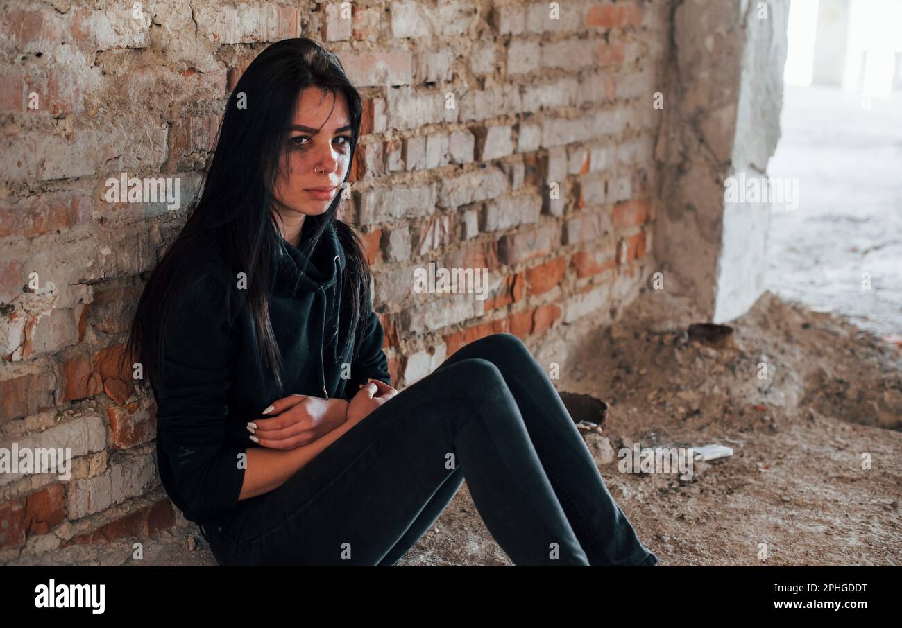 Young beaten woman in black clothes sitting on the floor of abandoned ...