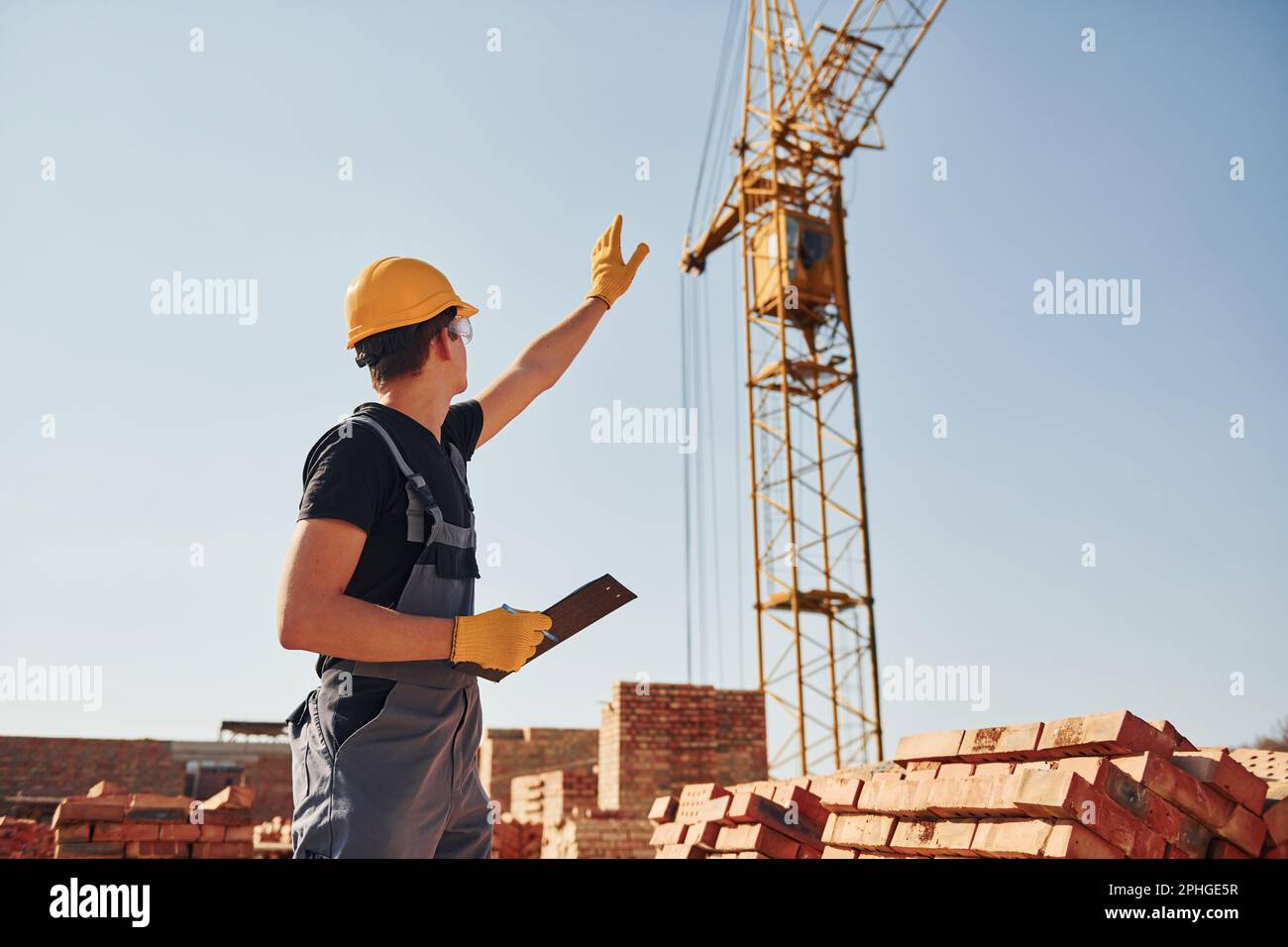 Communicating with crane guy. Construction worker in uniform and safety equipment have job on ...
