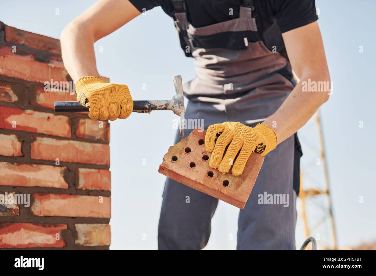 Holding brick and using hammer. Construction worker in uniform and ...