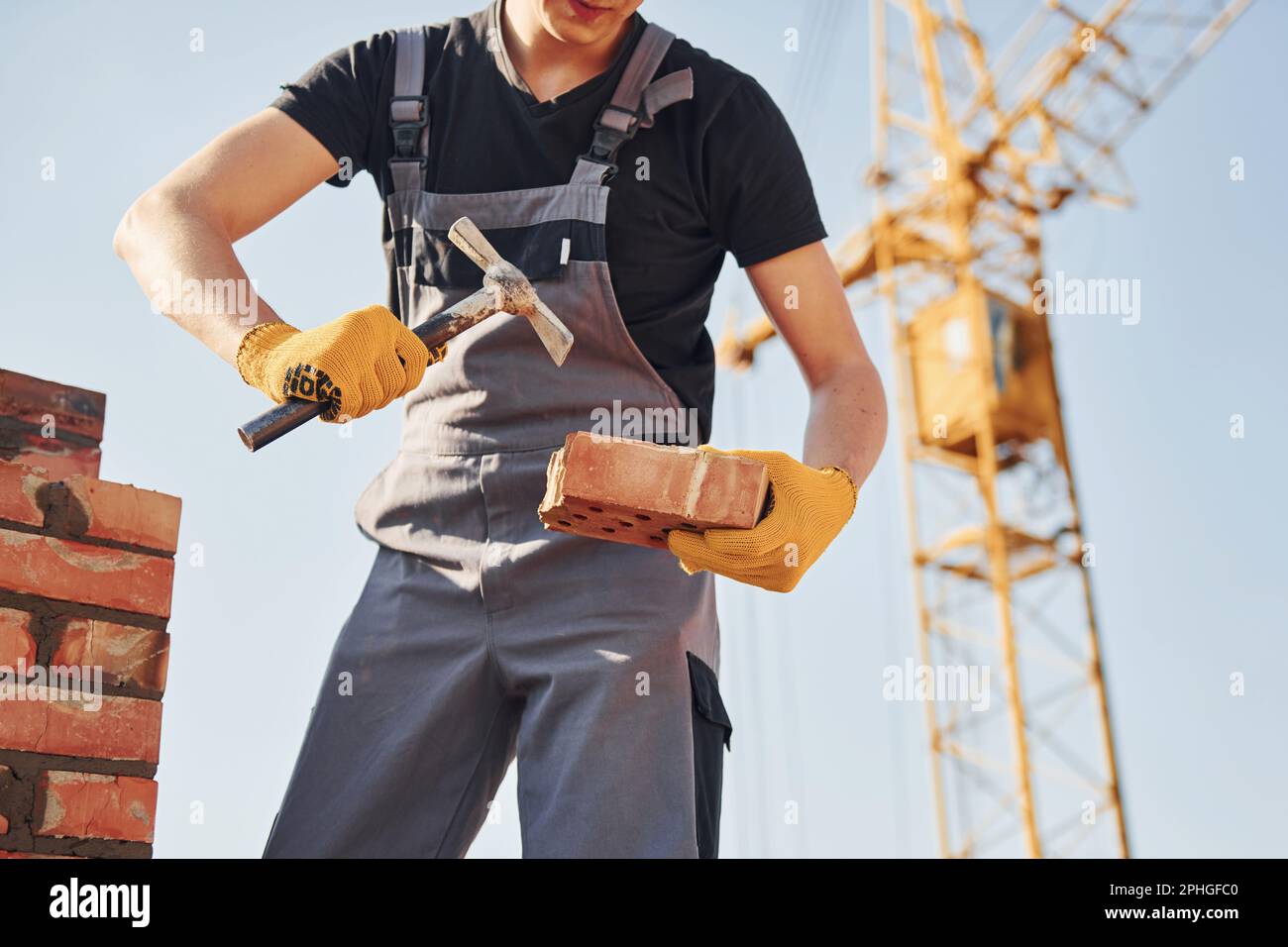 Holding brick and using hammer. Construction worker in uniform and ...