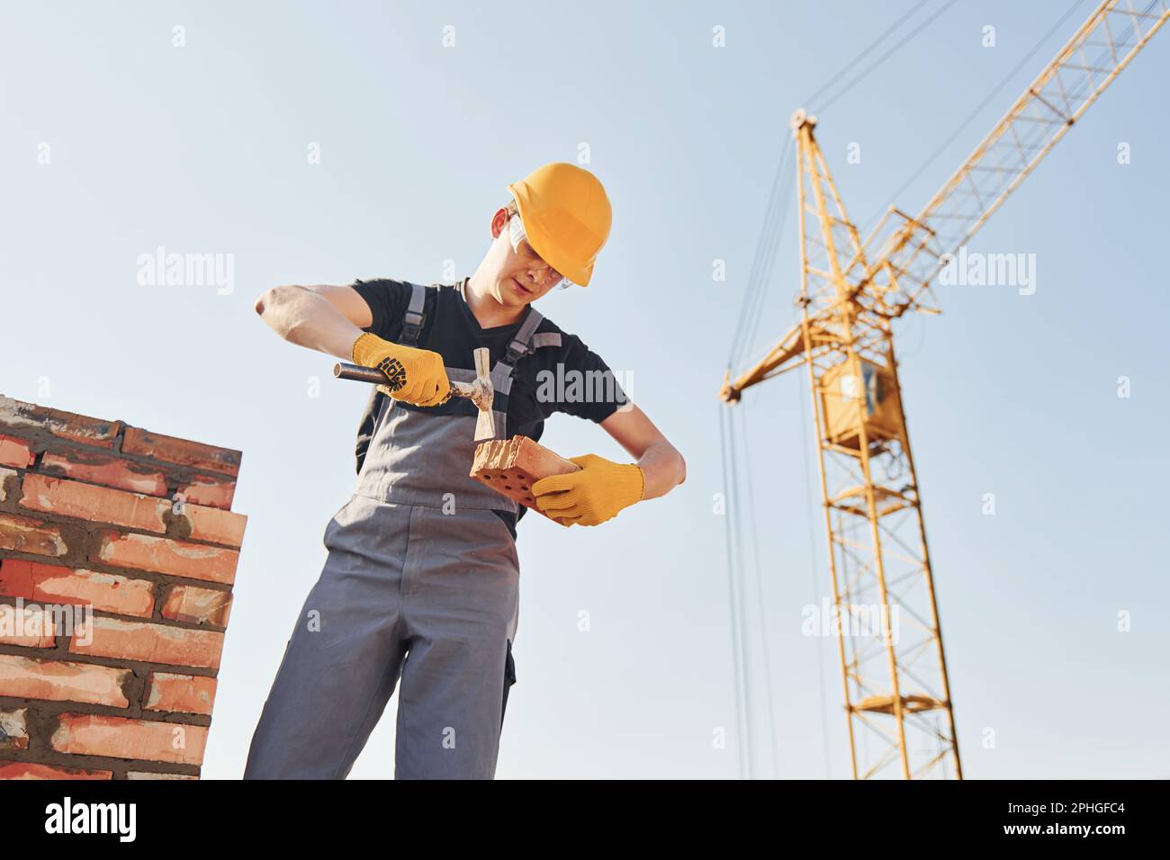 Holding brick and using hammer. Construction worker in uniform and ...