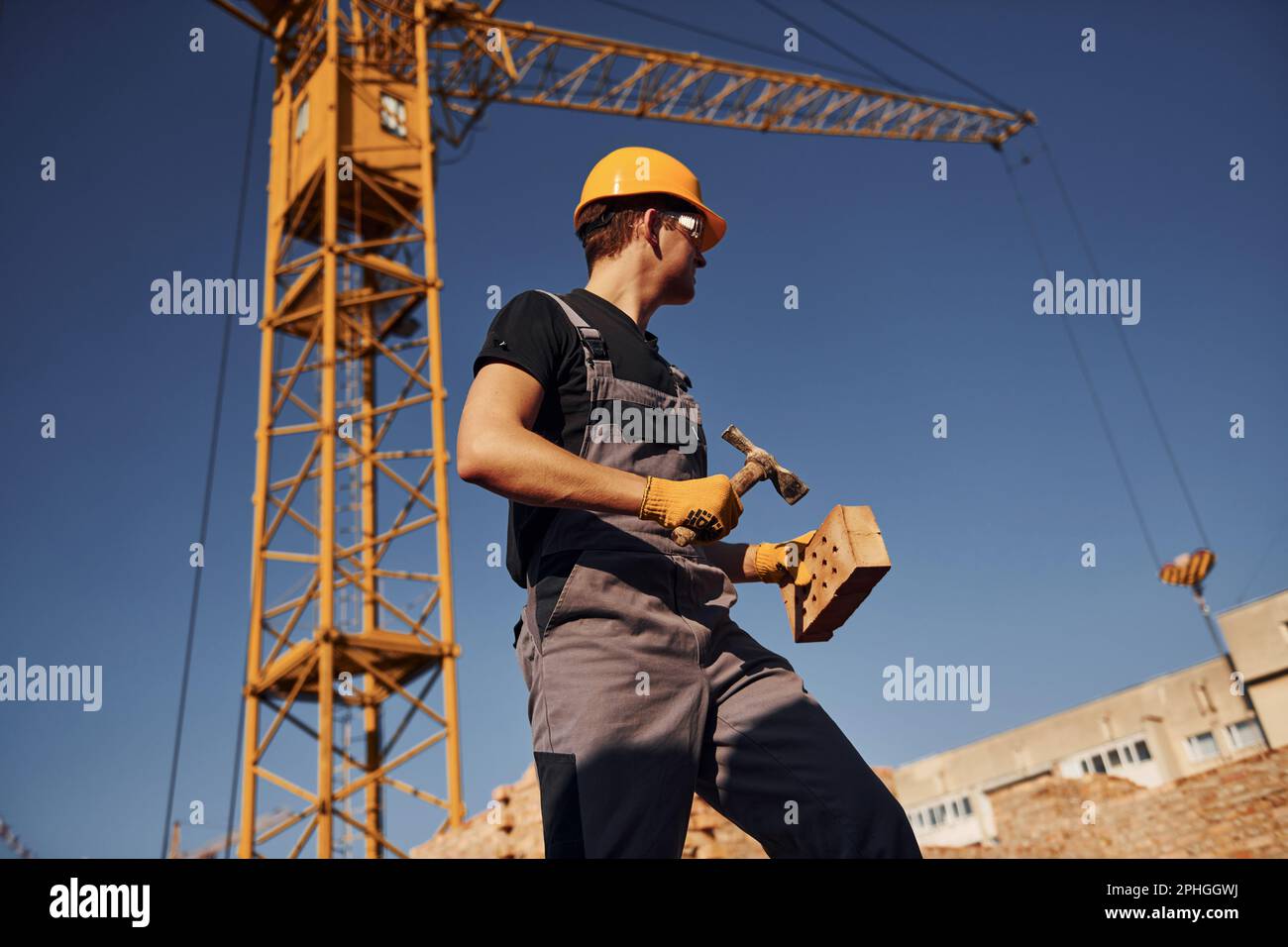 Holds brick and tool in hands. Construction worker in uniform and ...