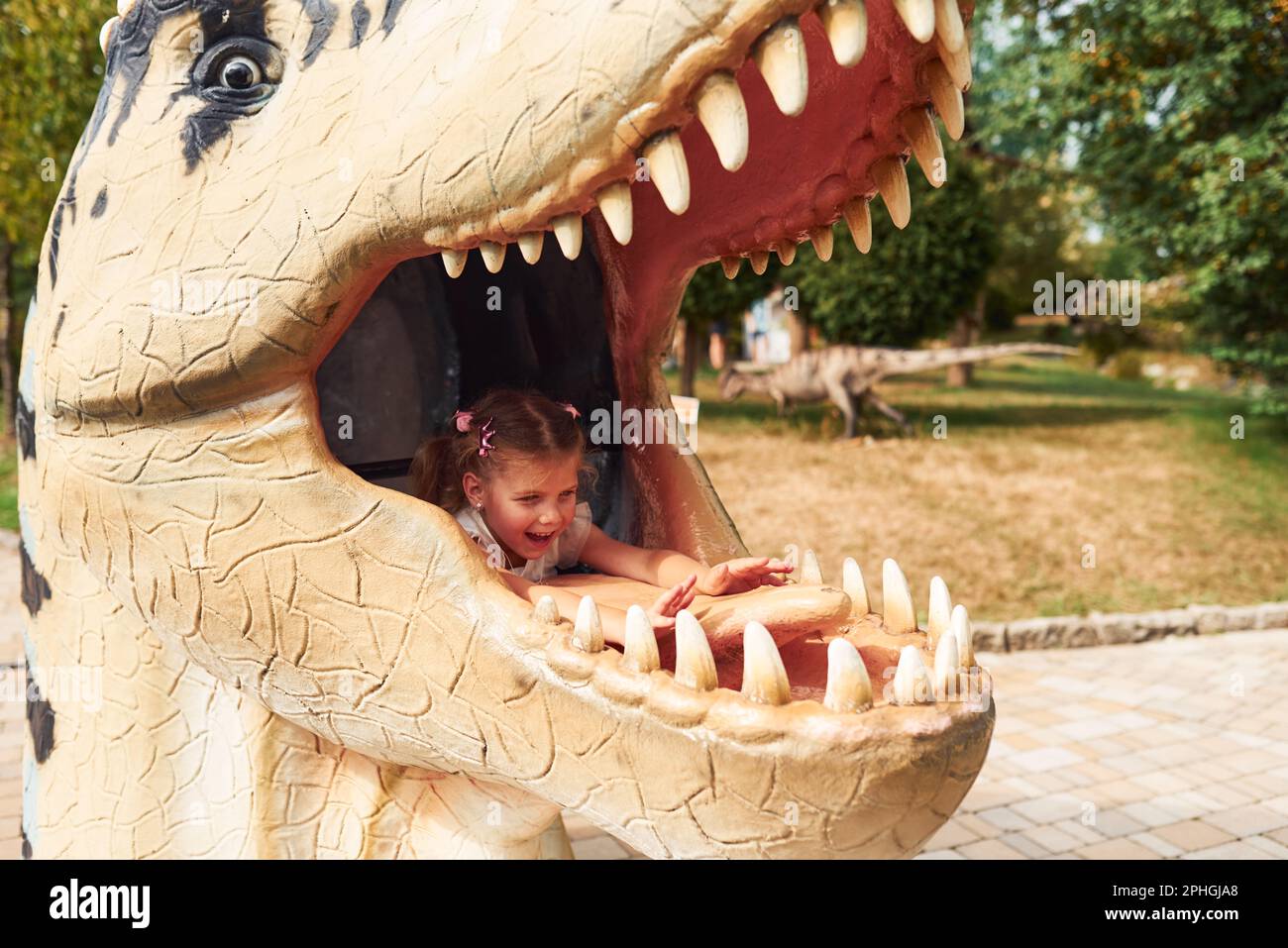 Cheerful little girl having fun in park with dinosaur replicas outdoors ...
