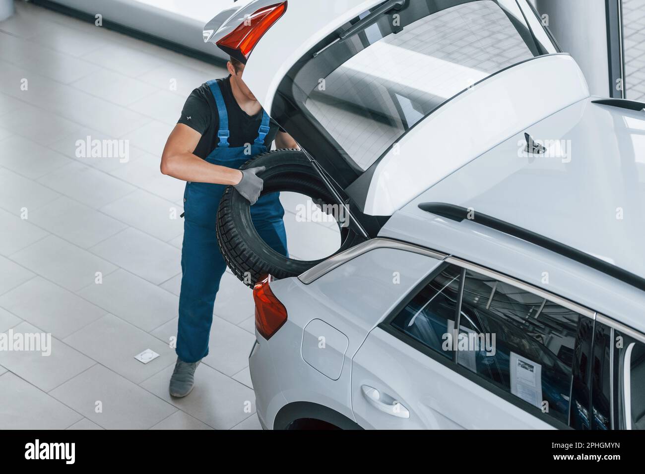 Worker in black and blue uniform places car wheel inside of white ...