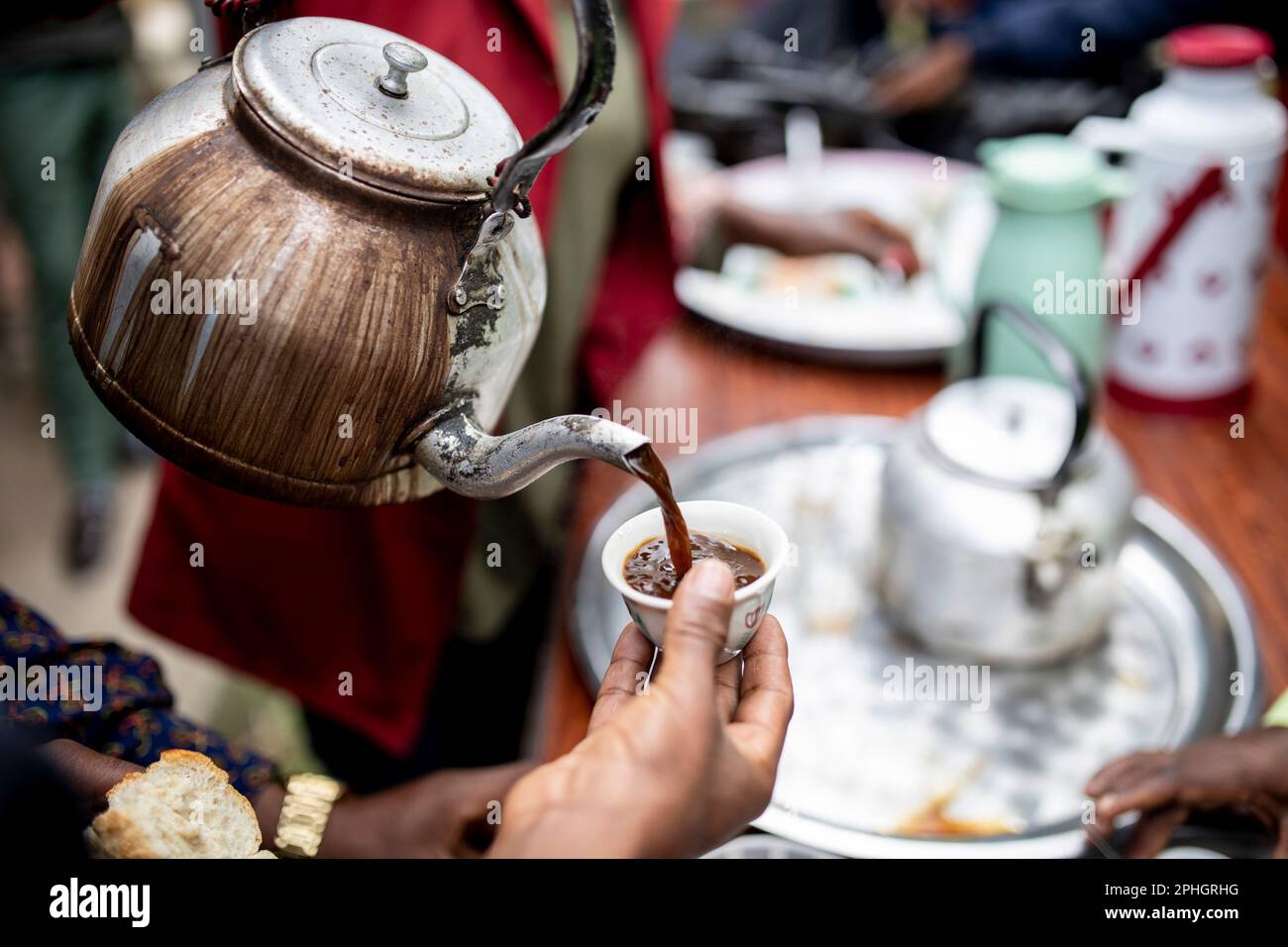 Pouring dark coffee from a communal pot into cups in Ethiopia Stock ...