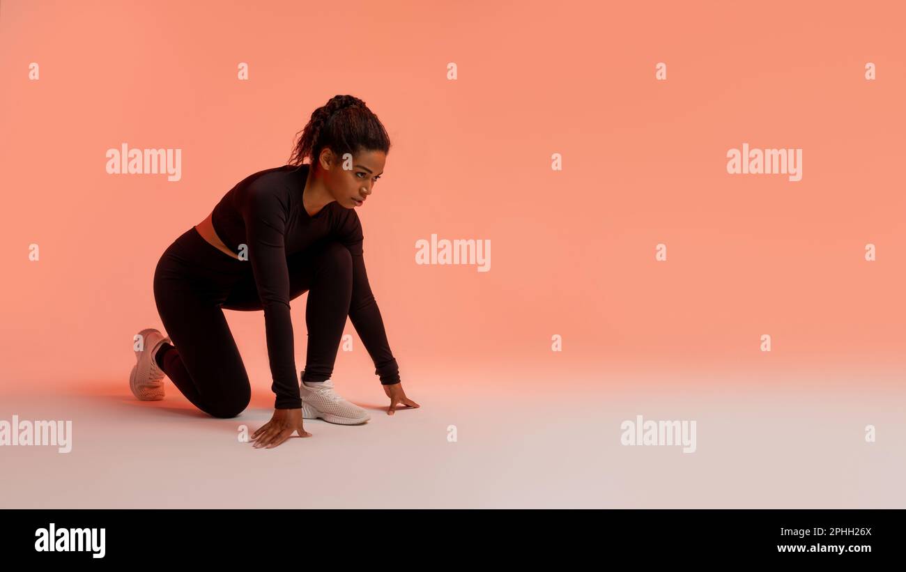 Motivated black female runner, standing in crouch start position, ready ...
