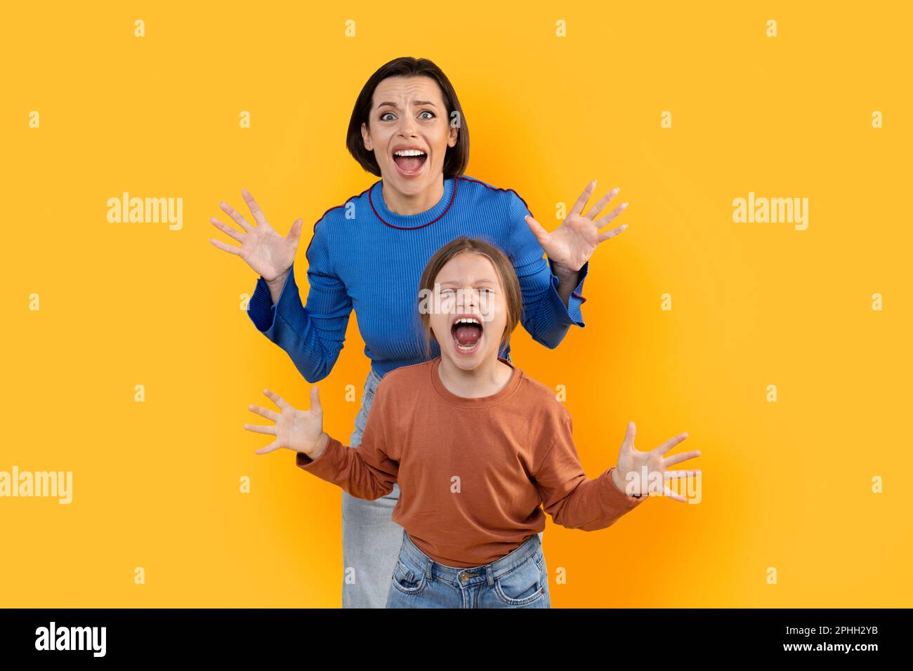Scared young mother and little daughter screaming on yellow background ...