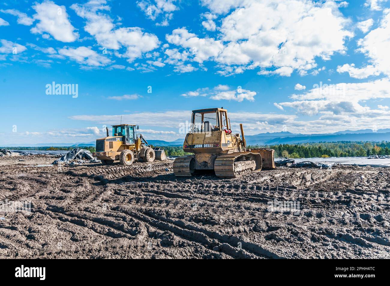 Two bulldozer tractors parked on dirt which has lots of tread tracks in ...