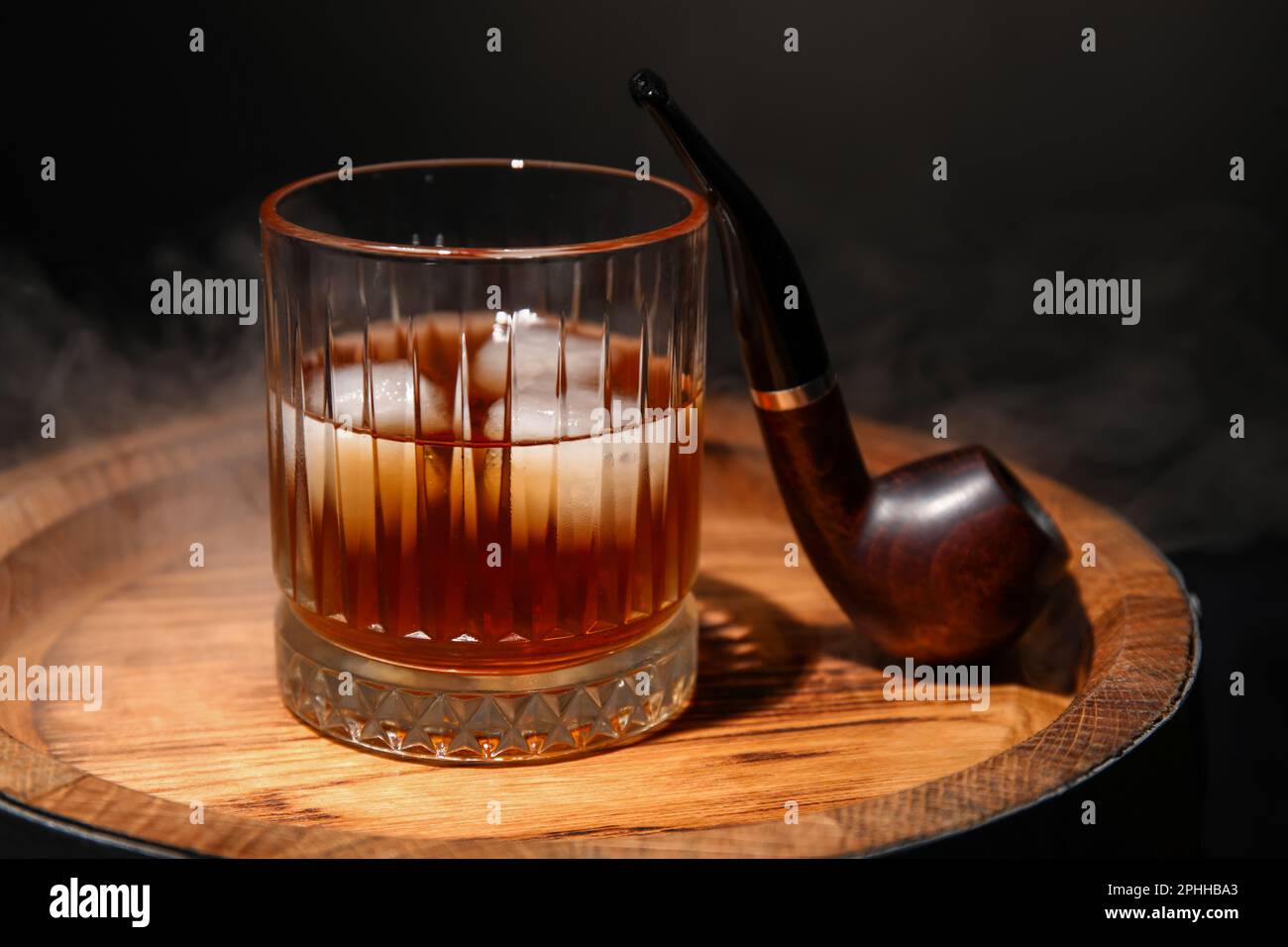 Wooden barrel with glass of cold rum and smoking pipe on dark ...
