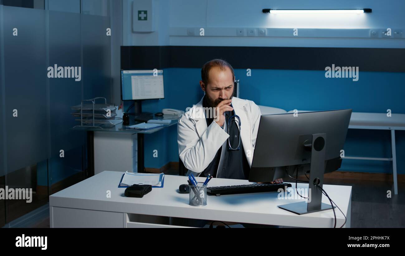 Tired physician doctor working late at night in hospital office typing ...
