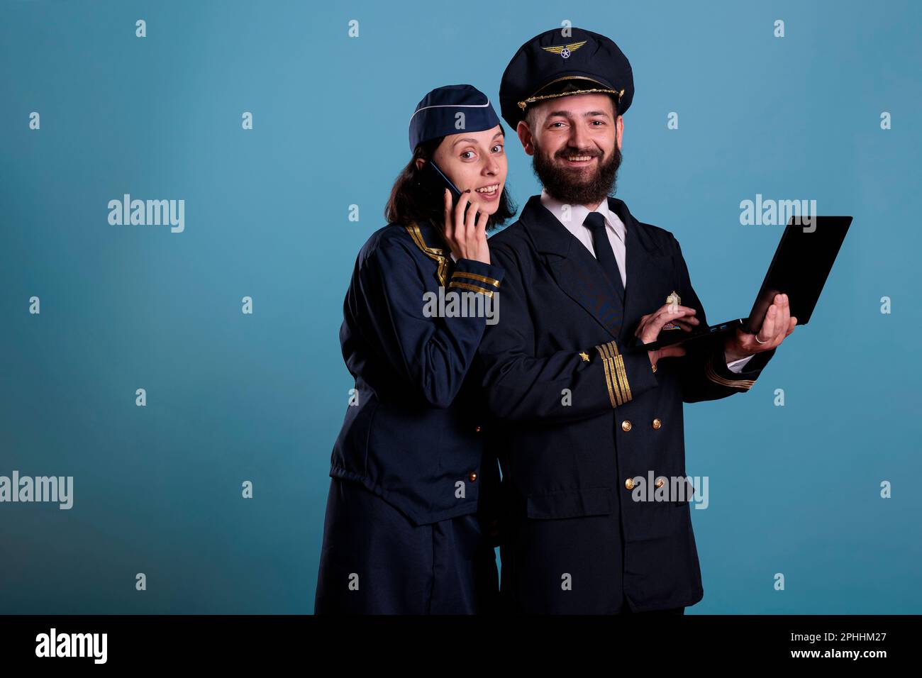 Smiling pilot using laptop, flight attendant talking on smartphone ...
