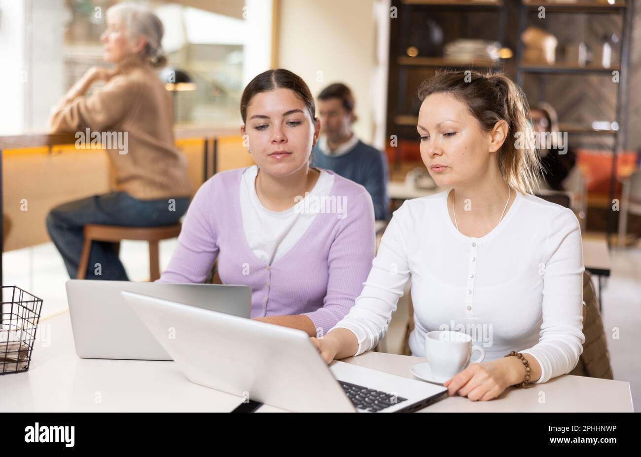 Two confident female cafe customers enjoying coffee while working on ...