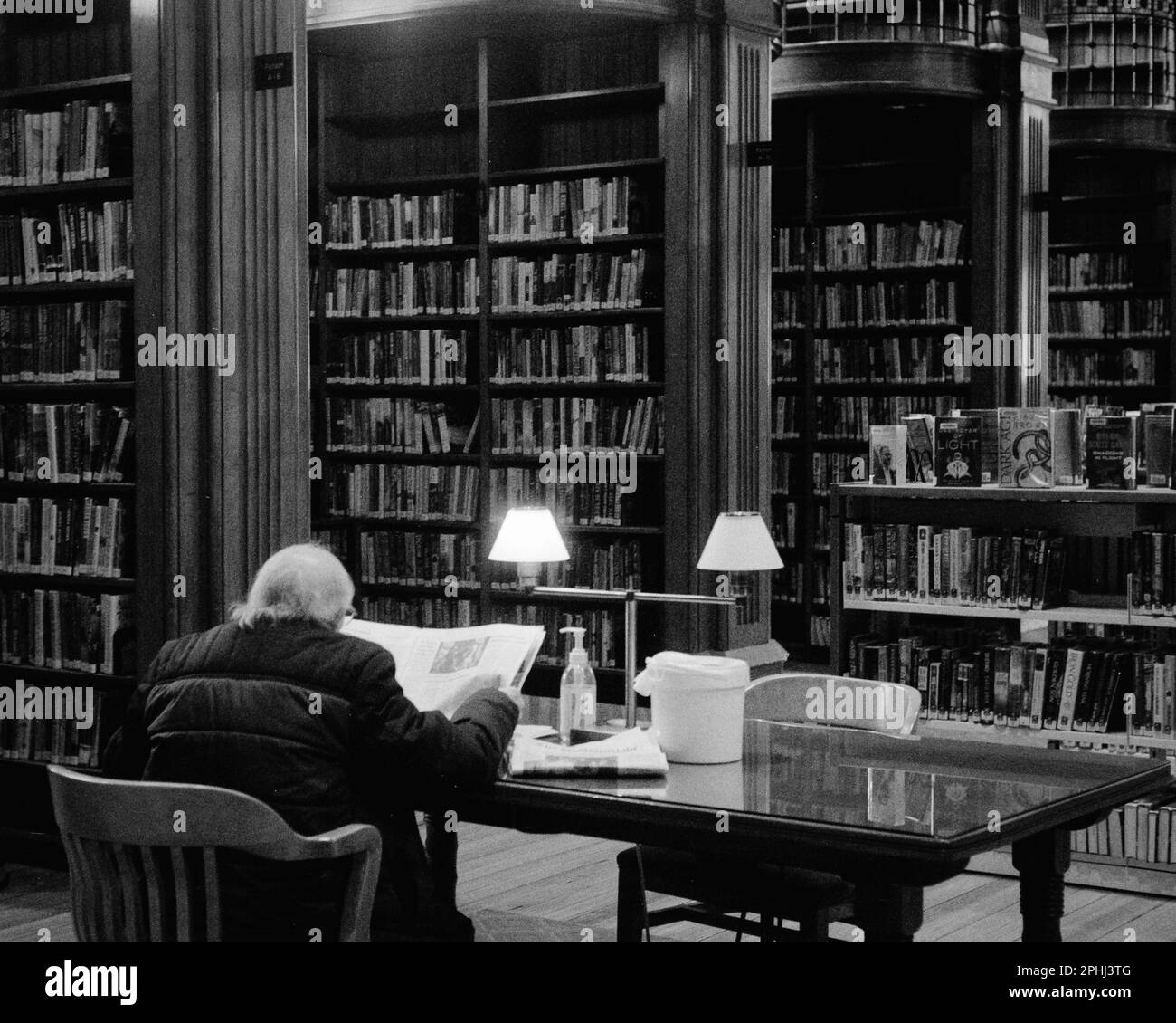 A man sits reading a newspaper at a table in the study hall of the ...