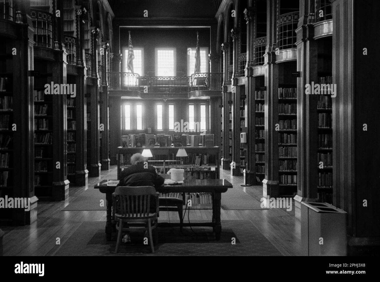 A man sits reading a newspaper at a table in the study hall of the ...